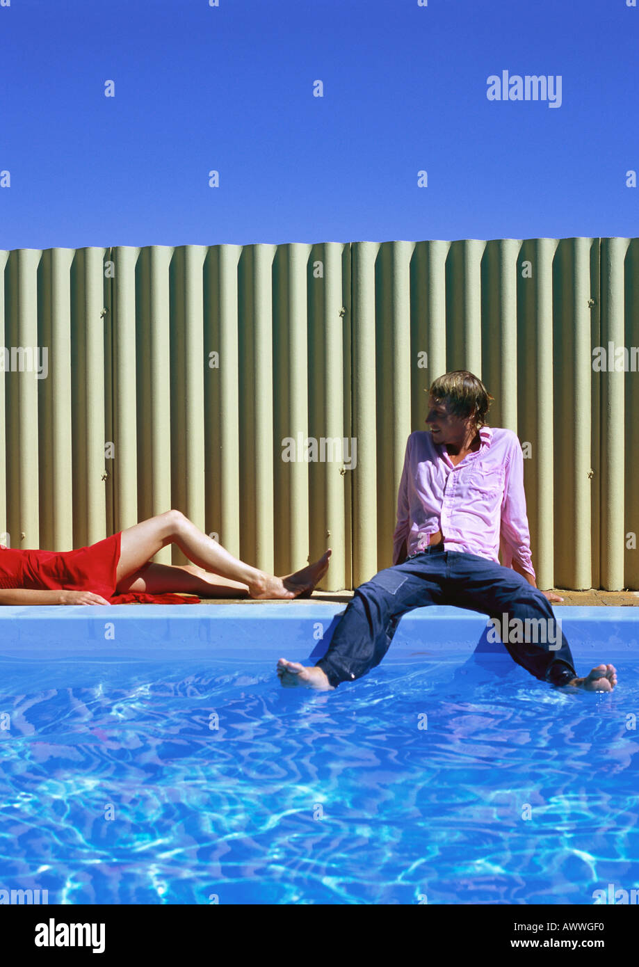 Man and woman relaxing by swimming pool, man dipping feet in water ...