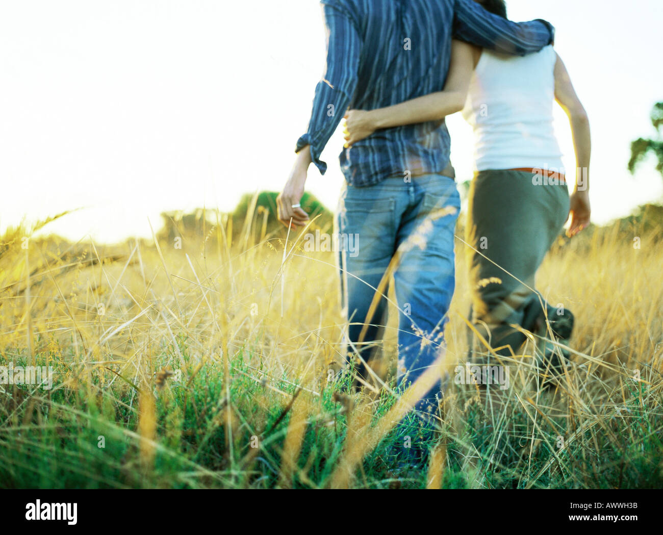 Couple walking through field, rear view, low section Stock Photo - Alamy
