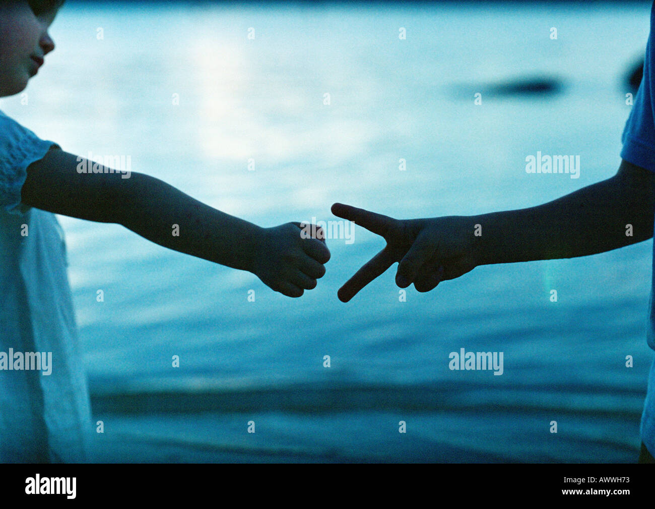 Children playing 'rock paper scissors', close-up, sea in background ...