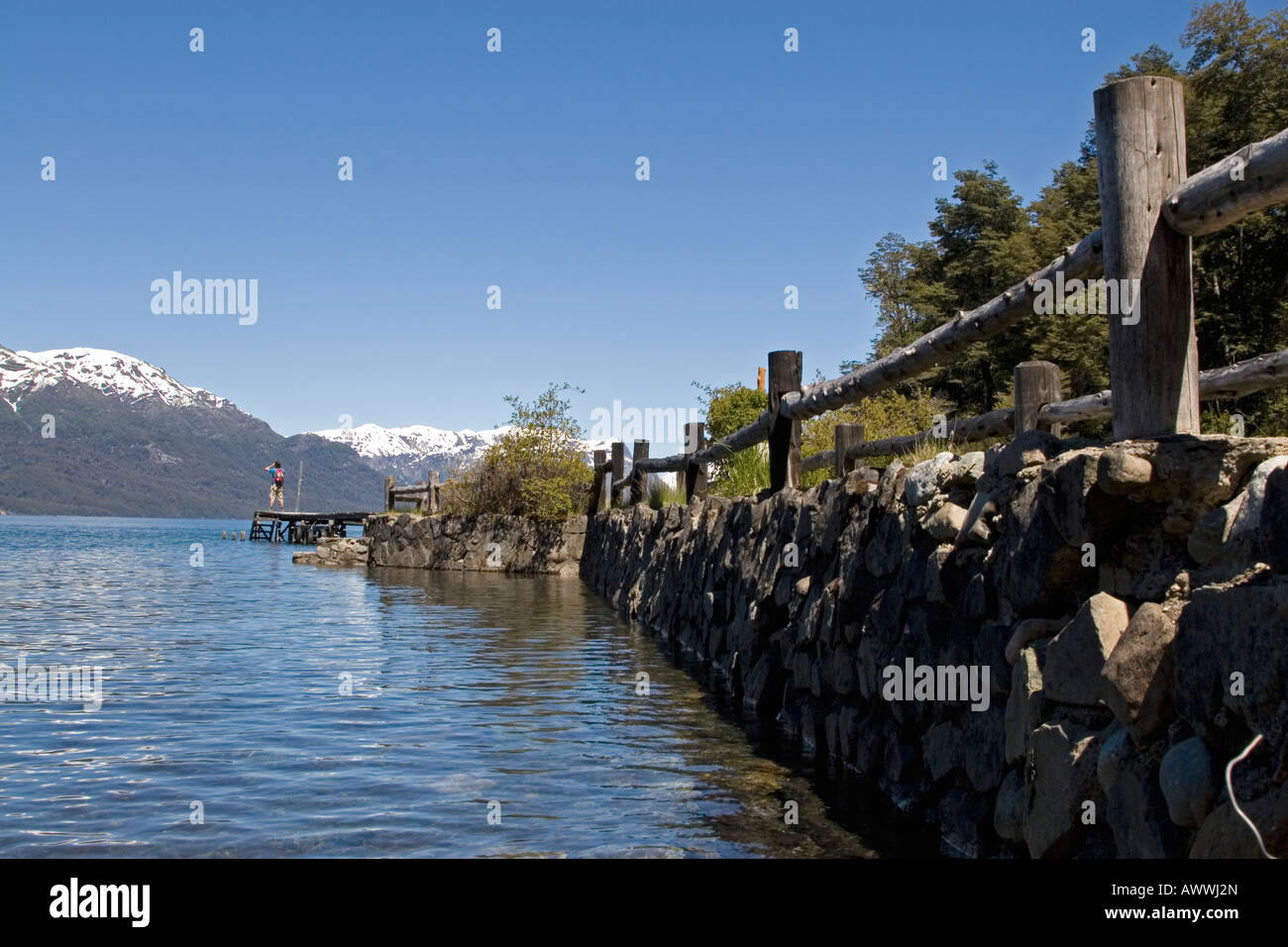 Distant male figure stood on end of lake jetty taking photograph of ...