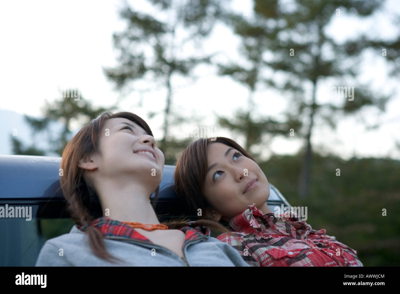 Two young women leaning on car and looking up Stock Photo - Alamy