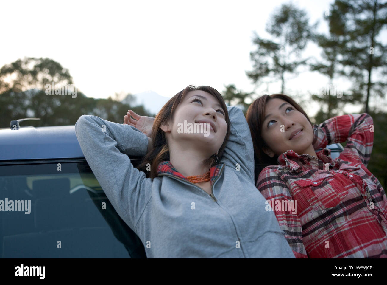 Two young women leaning on car and looking up Stock Photo - Alamy