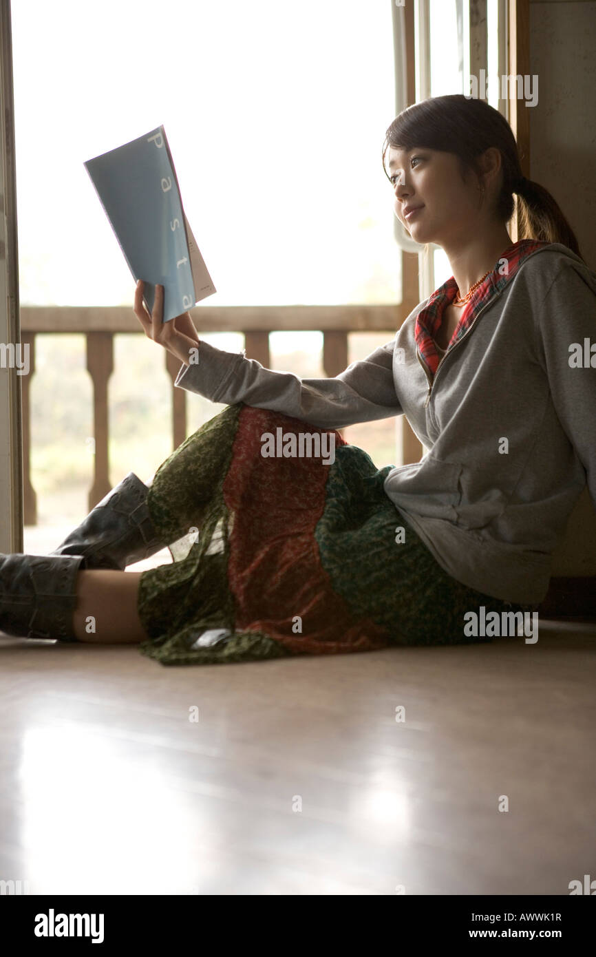 Young woman sitting on floor and reading book Stock Photo - Alamy