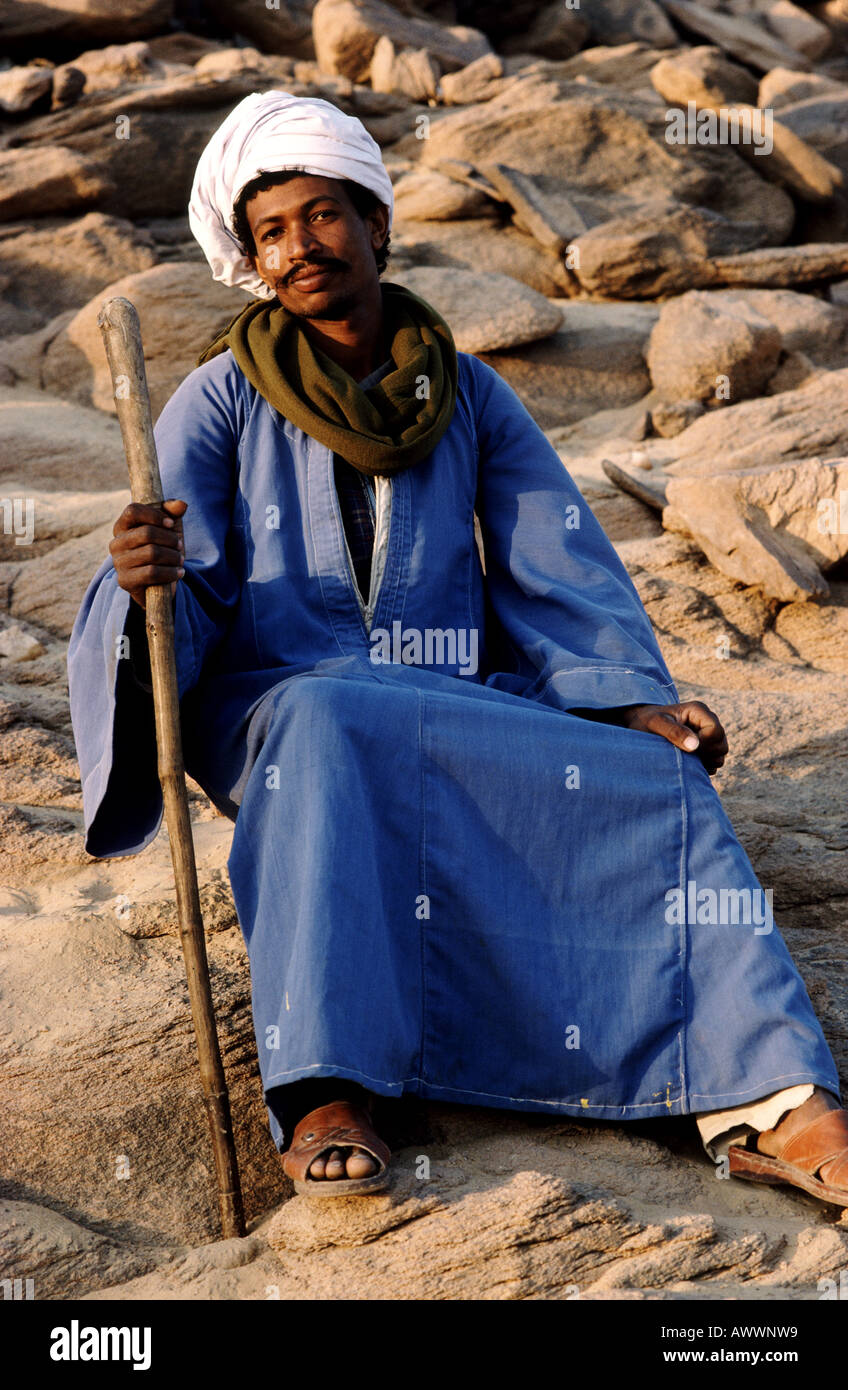 A young Arab shepherd in a blue robe with a staff sits patiently on a ...