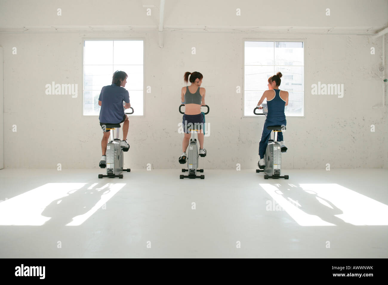 Three friends on exercise bikes in gym, rear view Stock Photo - Alamy