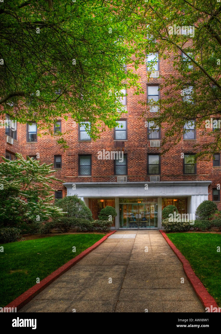 brick apartment building with lush green trees and lobby lit up Stock ...