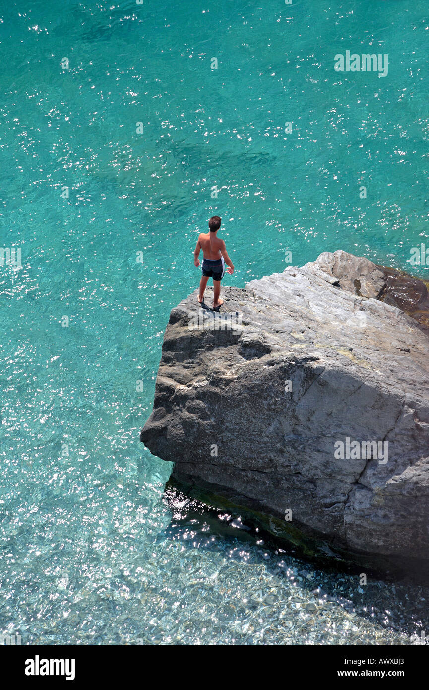 Aerial photo of young boy standing on rock looking into deep blue ocean ...