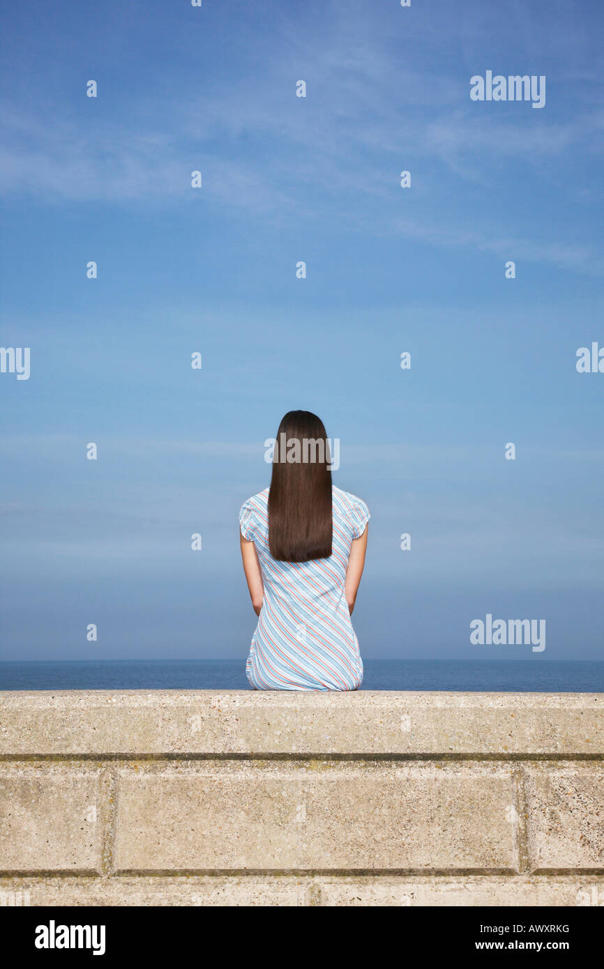Young woman sitting on stone ledge, back view Stock Photo - Alamy