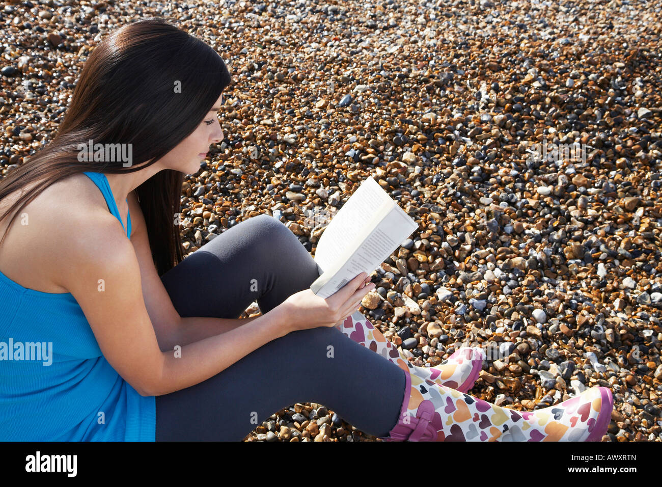 Young woman sitting on beach reading book, side view Stock Photo - Alamy