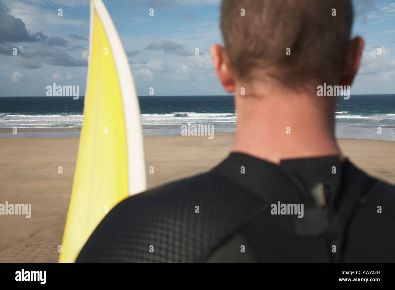 Man holding surfboard on beach looking at sea, back view, close up ...