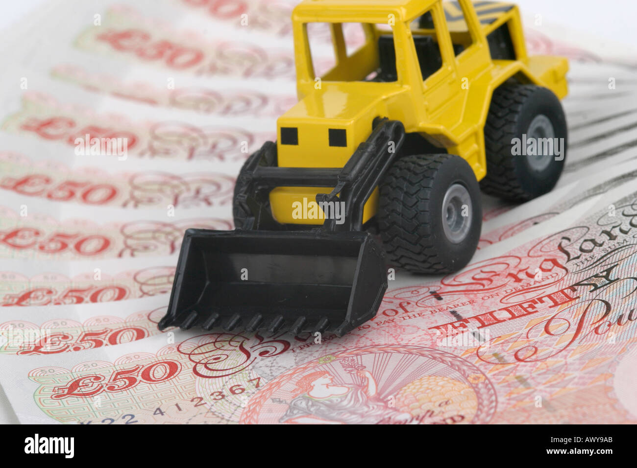 bulldozer digger on a pile of fifty pound notes on a white background ...