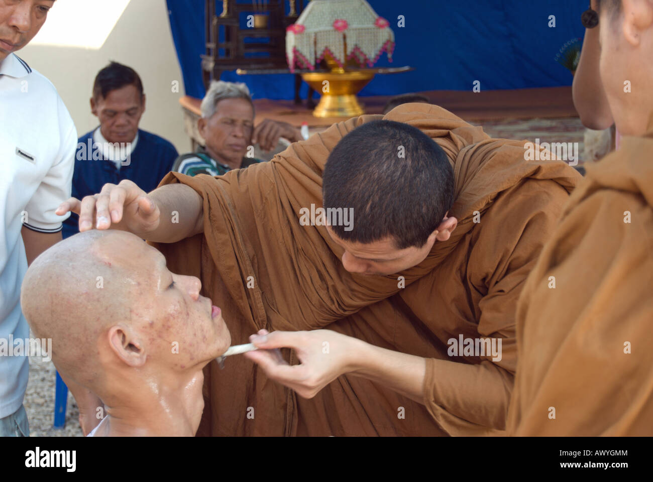 as family members watch, a thai buddhist monk shaves the chin of a ...