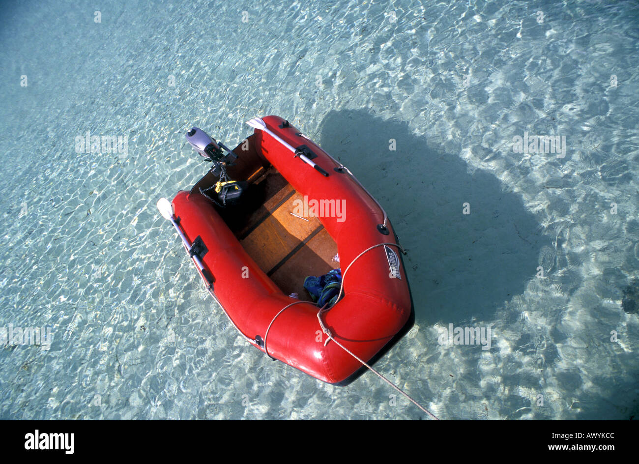 Small red inflatable boat zodiac floating in clear shallow tropical ...
