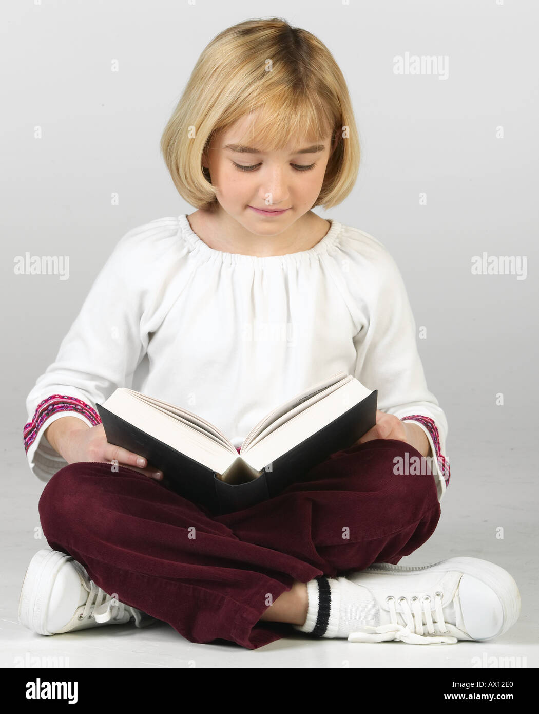 Caucasian blonde girl sitting cross legged and reading from a book ...