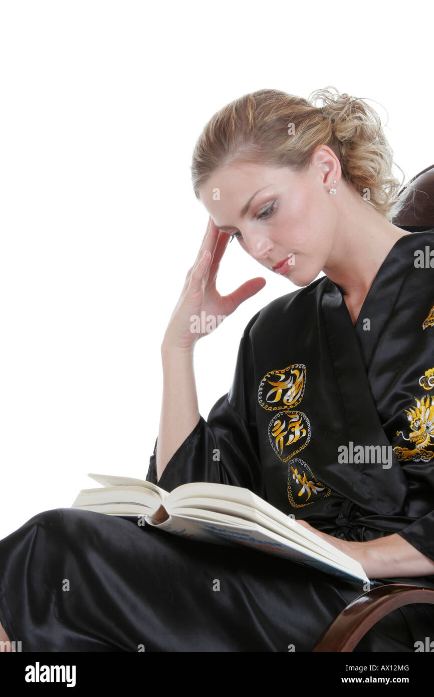 Young woman wearing kimono bath robe sitting on chair reading book ...