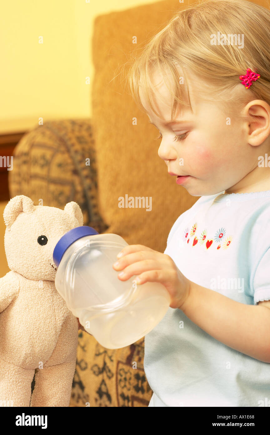Little girl giving her teddy bear a drink Stock Photo - Alamy