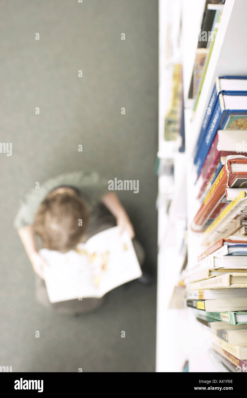 Little boy reading book beside library shelf 1 Stock Photo - Alamy
