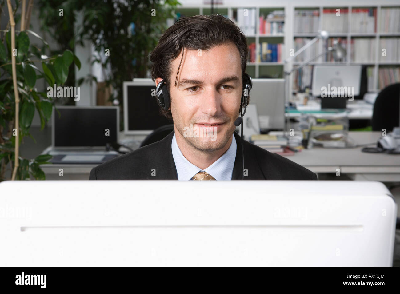 A man wearing a telephone headset and working on a computer Stock Photo ...