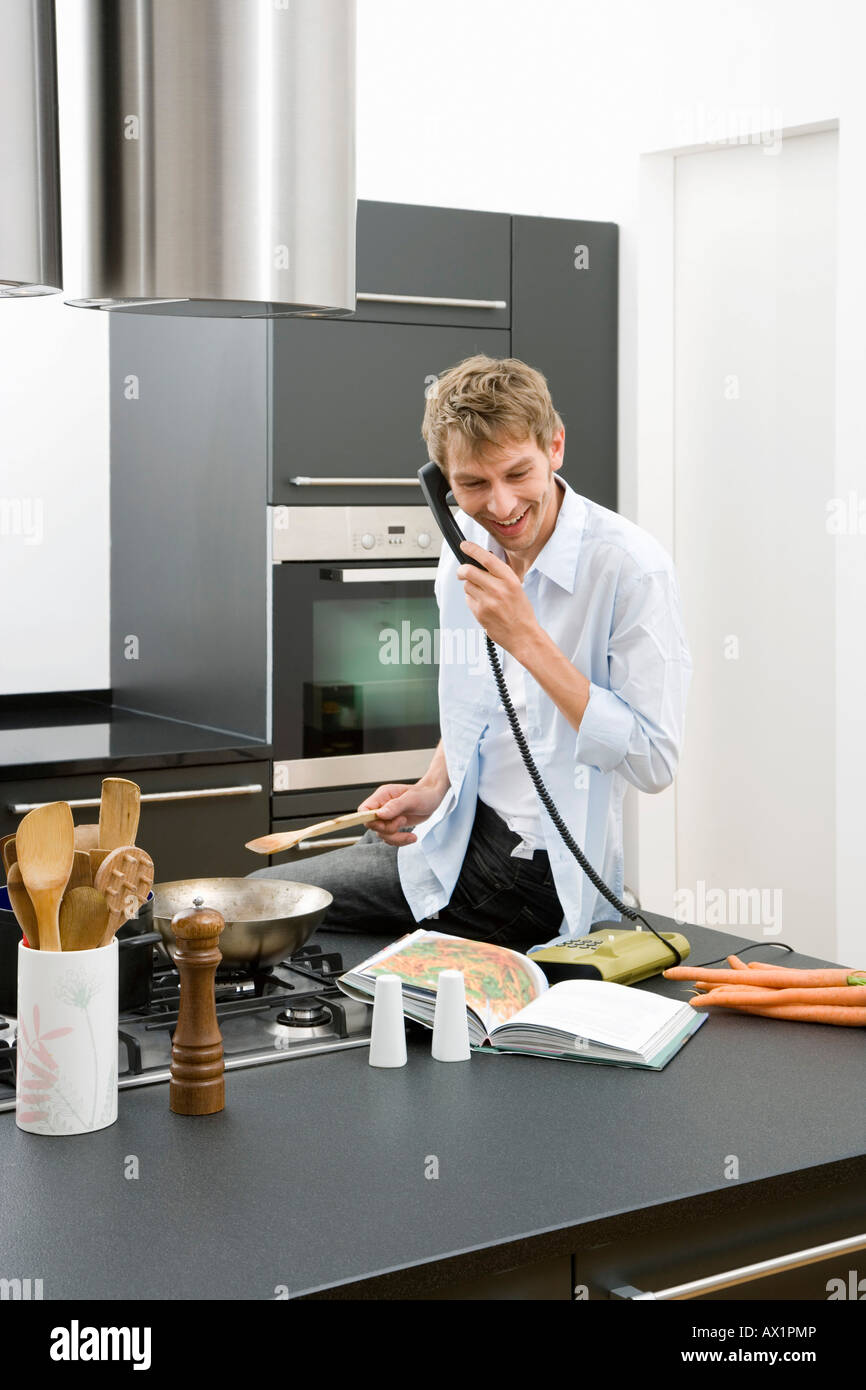 A man sitting on a kitchen worktop and using the telephone Stock Photo ...