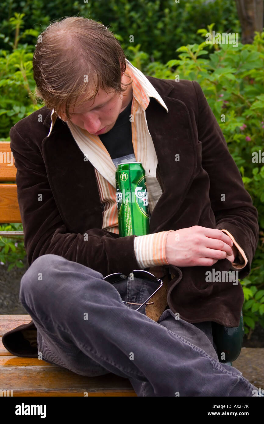 Alcoholic young man in his 20's drinking Carlsberg lager on park bench ...