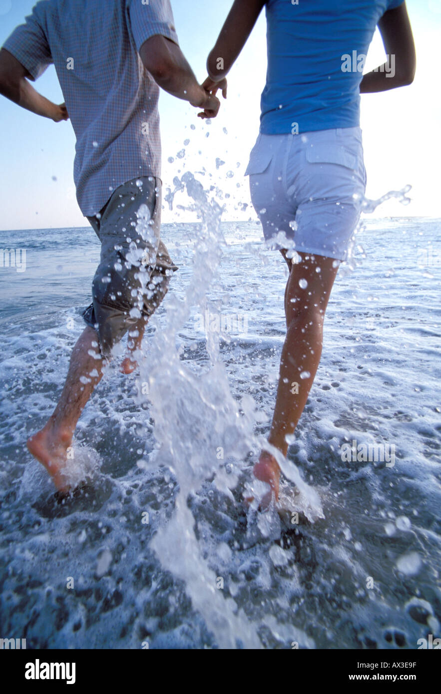 Couple on beach running over water edge wave Stock Photo - Alamy