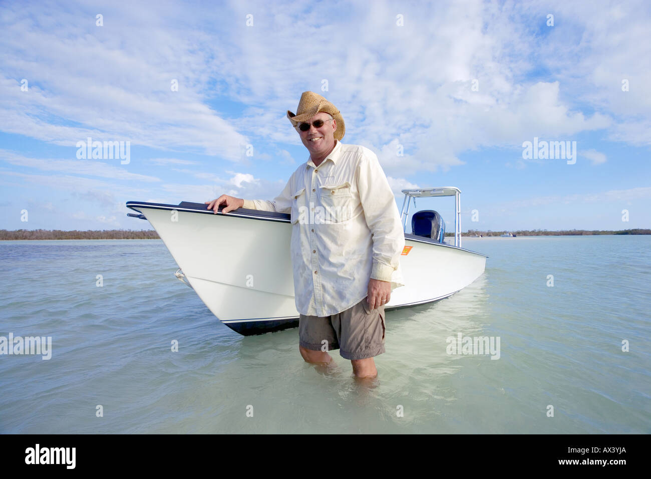 Saltwater fishing guide standing in shallow water in front of his boat ...