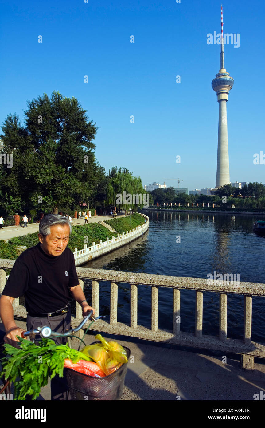 China, Beijing. A man walking his bicycle over a bridge near the CCTV ...