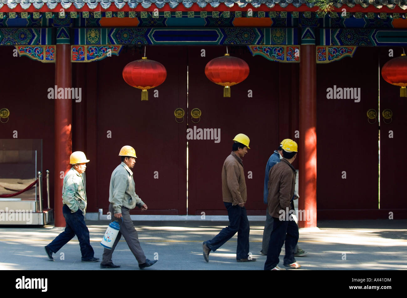 China, Beijing. Construction workers walking past a temple entrance ...