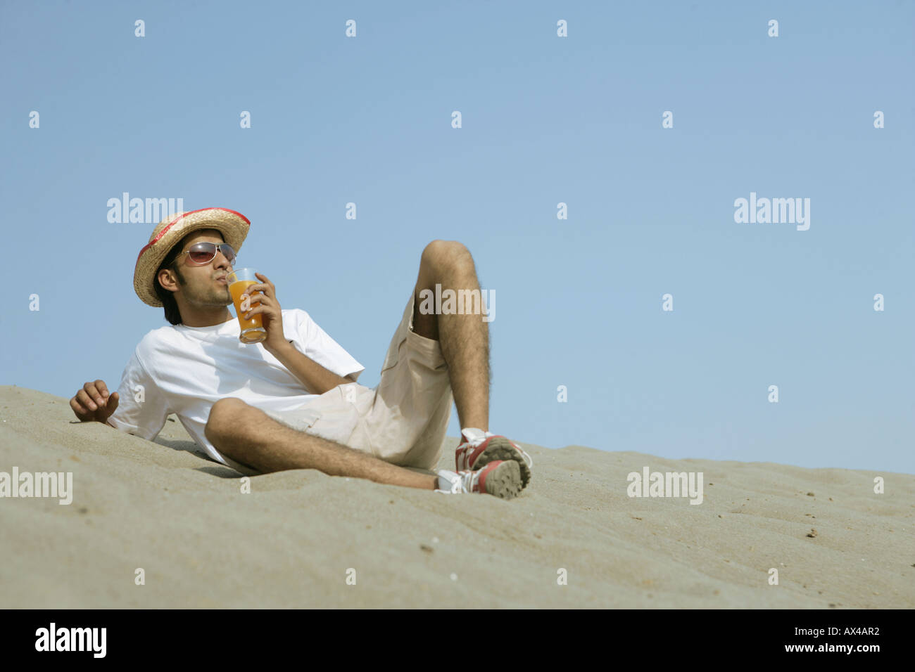 Man sitting on sand in a desert and drinking juice Stock Photo - Alamy
