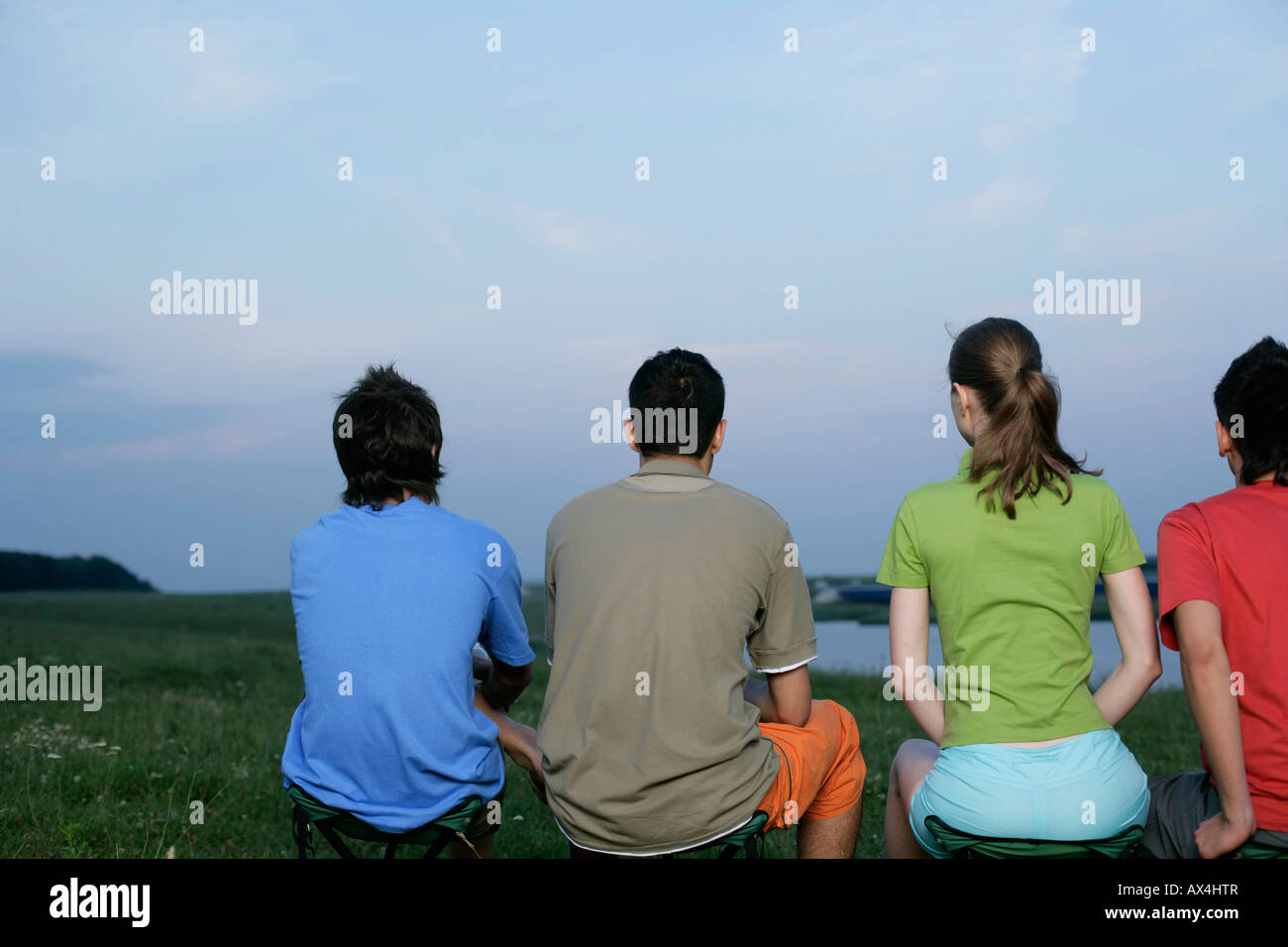 Four young people sitting in a line Stock Photo - Alamy