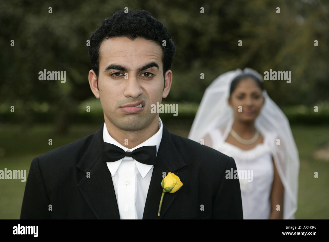 Portrait of a unsatisfied groom making a face with his bride standing ...