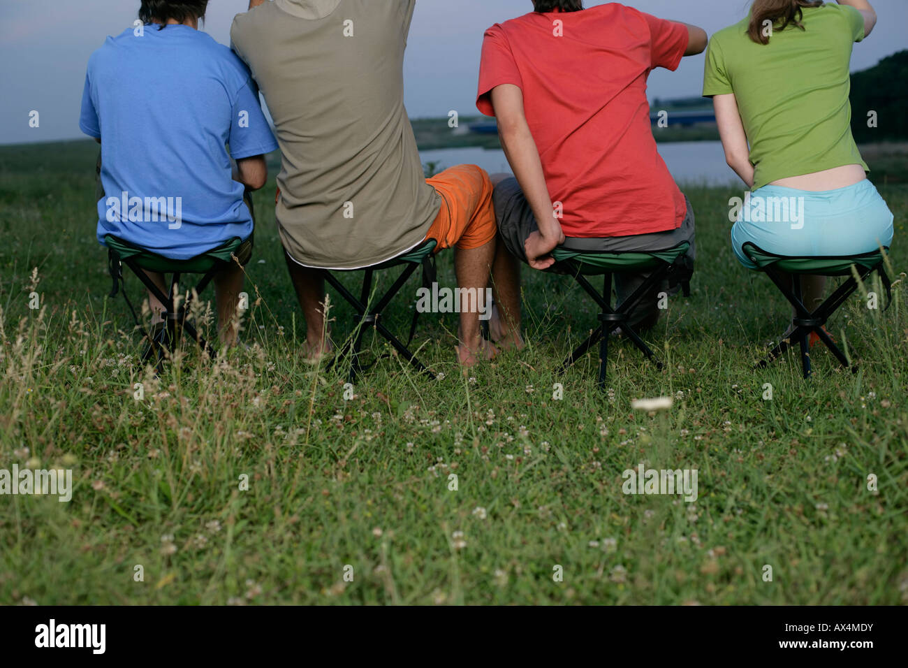 Four young people sitting in a line Stock Photo - Alamy