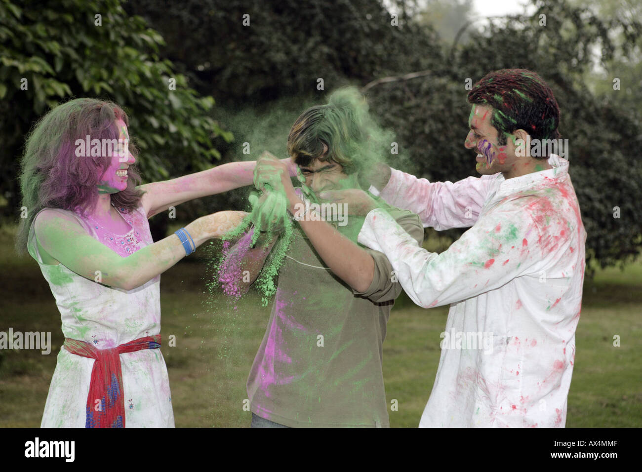 Three friends playing holi in a park Stock Photo - Alamy