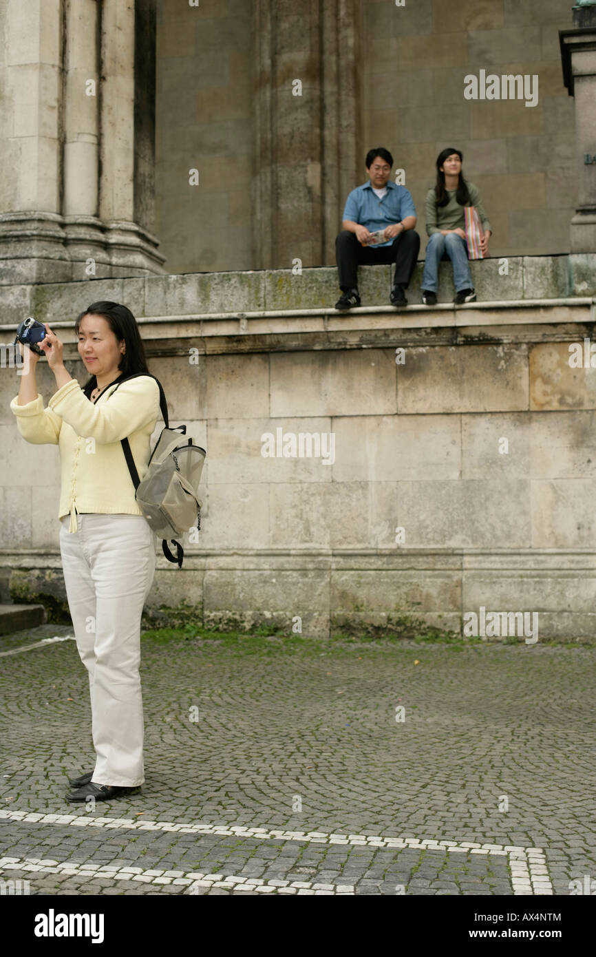 Asian woman with a camera standing in front of two sitting people Stock ...