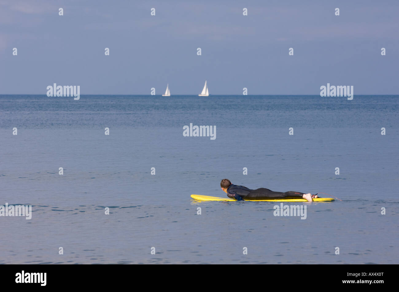 Surfer laid on a yellow surf board at Cayton Bay waiting for the waves ...