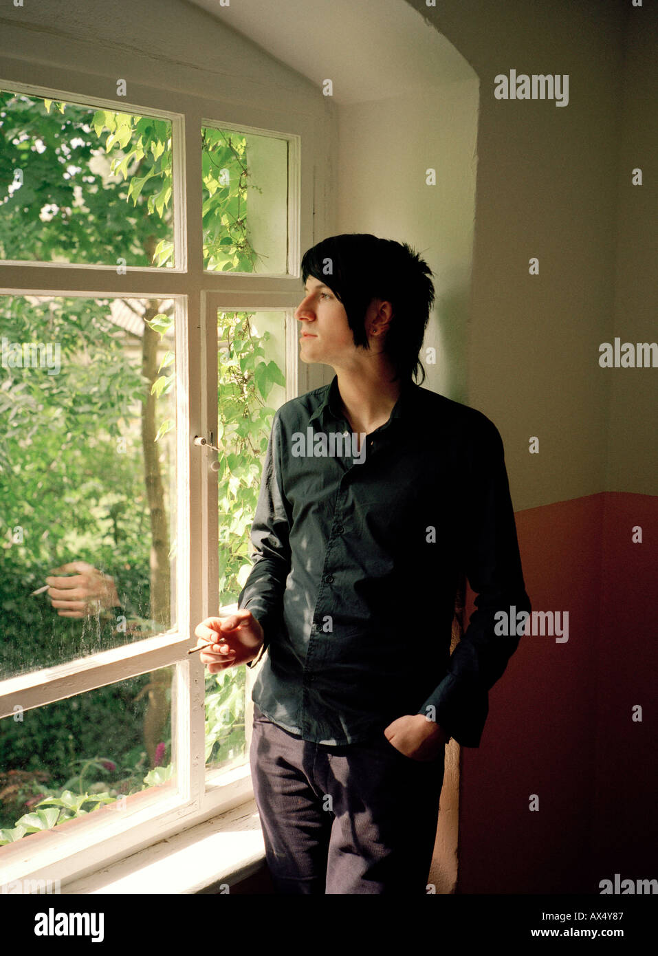 A man holding a cigarette looking out a window Stock Photo - Alamy