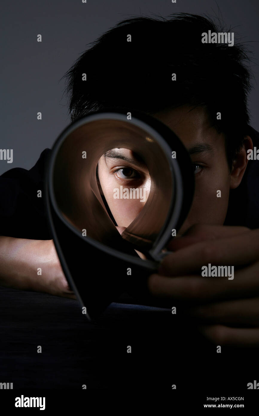 Young man looking through a rolled up magazine Stock Photo - Alamy