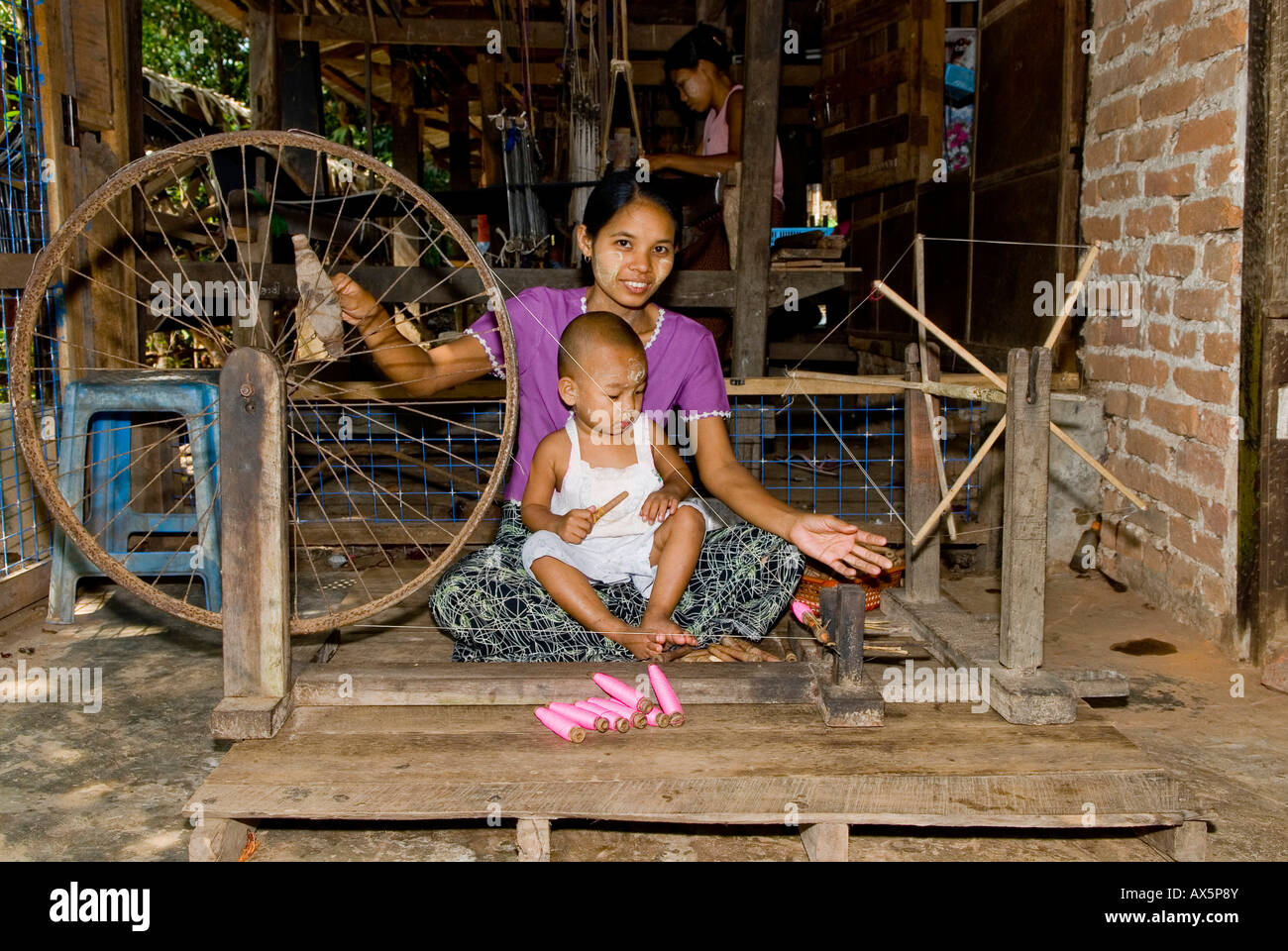 Burmese woman and her baby in front of a spinning wheel, Yangon ...