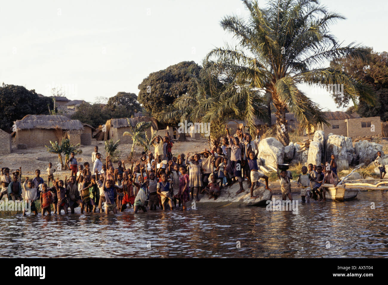 Kalepo, Tanzania. Village children knee-deep at the water's edge waving ...