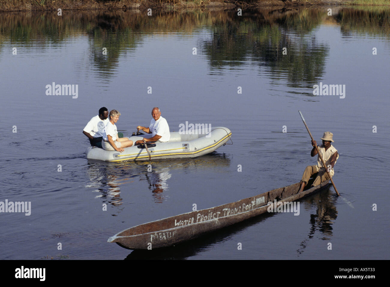 Zambia, Africa. Tourists in an inflatable dinghy greeting a man in a ...