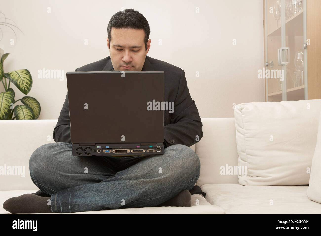 Young man sitting on couch with laptop Stock Photo - Alamy