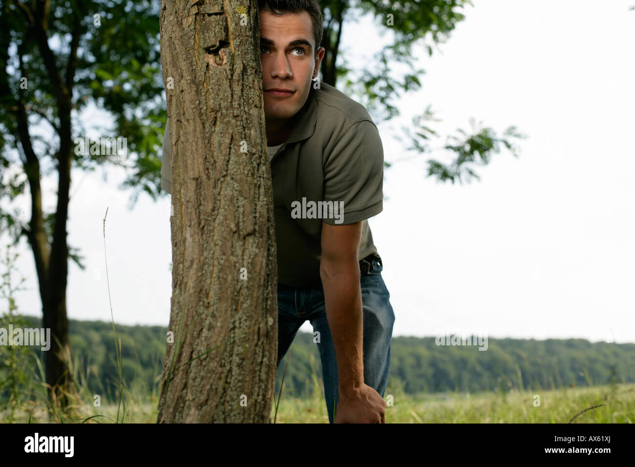 Mid adult man standing behind a tree Stock Photo - Alamy
