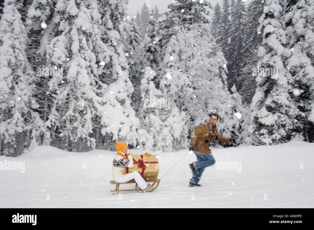 Man pulling woman holding present on sledge, side view Stock Photo - Alamy