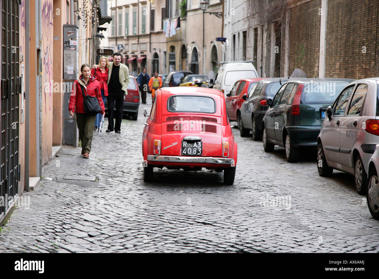 Red Fiat cinque cento driving down centre of cobbled street in Rome ...