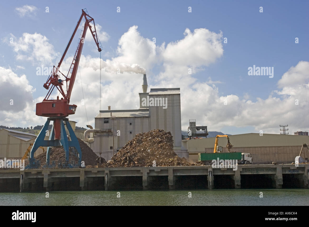 Crane on quayside unloading scrap metal into trucks for reprocessing ...