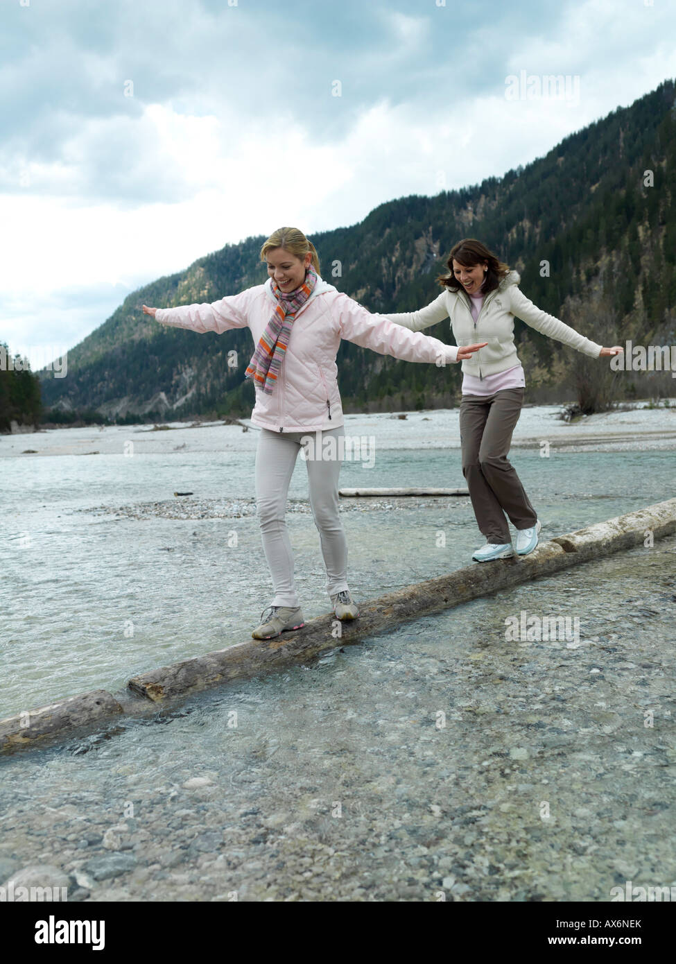 Two young women balancing on log in river Stock Photo - Alamy