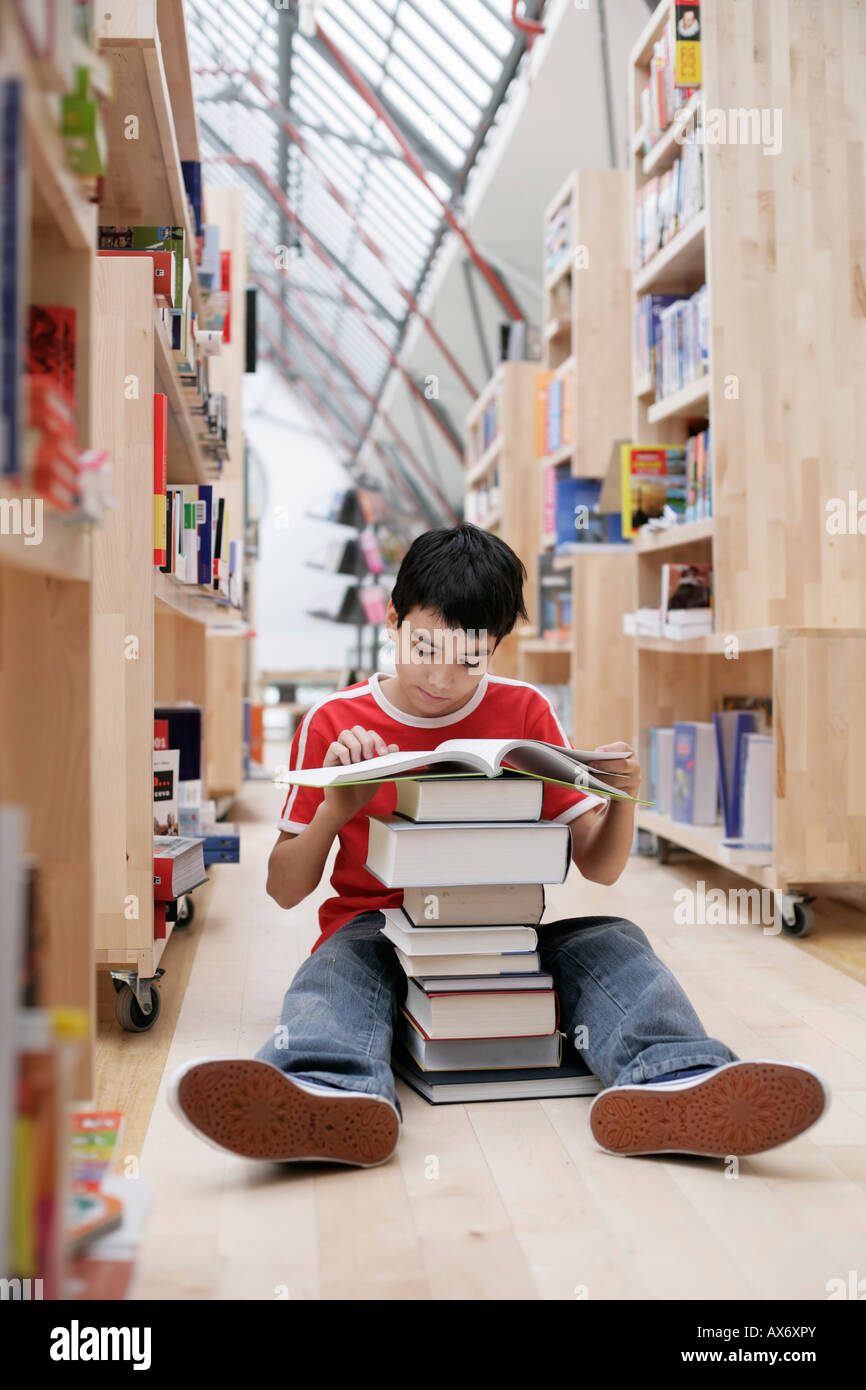 Boy reading a book next to a pile of books inside a library, fully ...