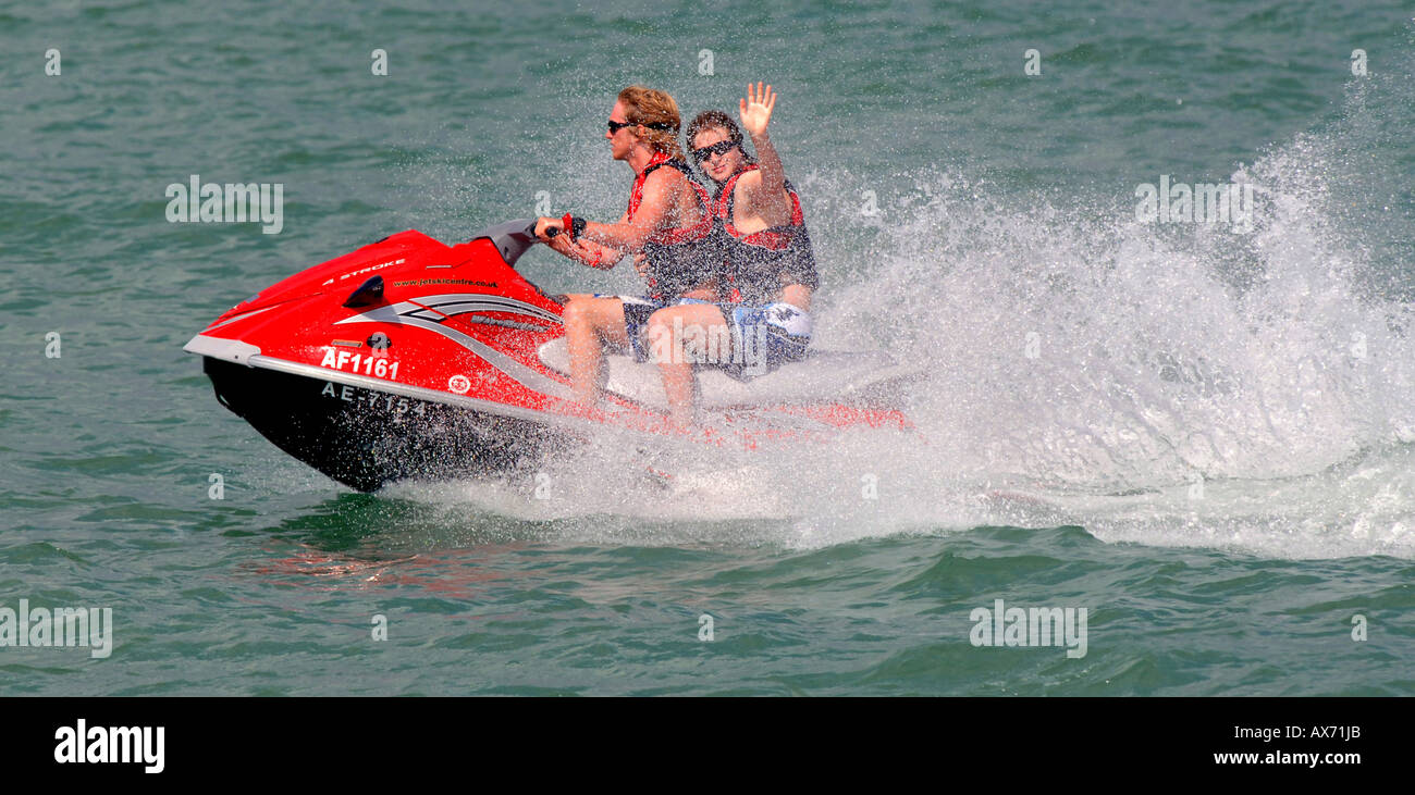 A couple speed past on a bright red jet ski on the South Coast, UK ...