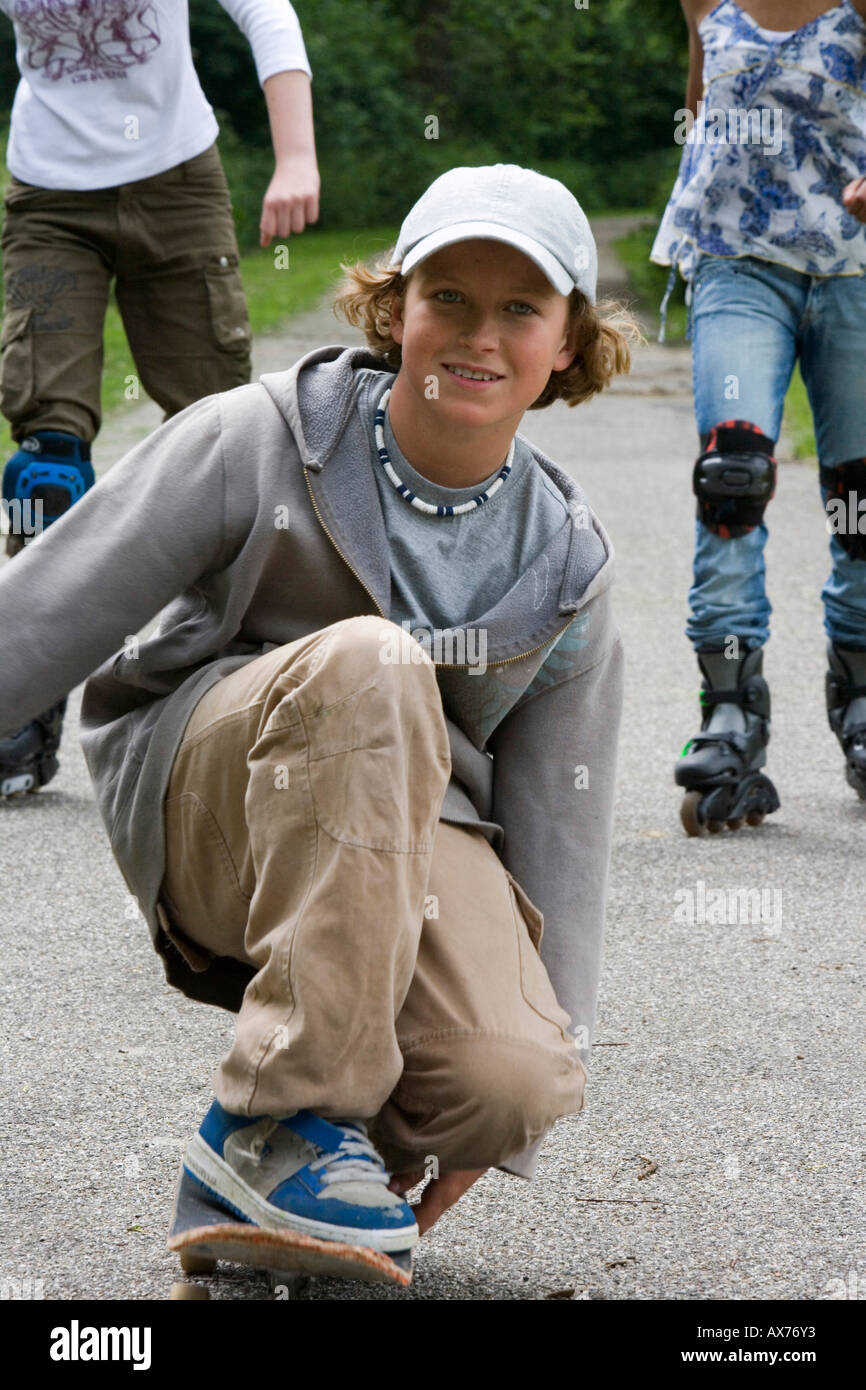 Portrait of a boy crouching on a skateboard and two girls inline ...