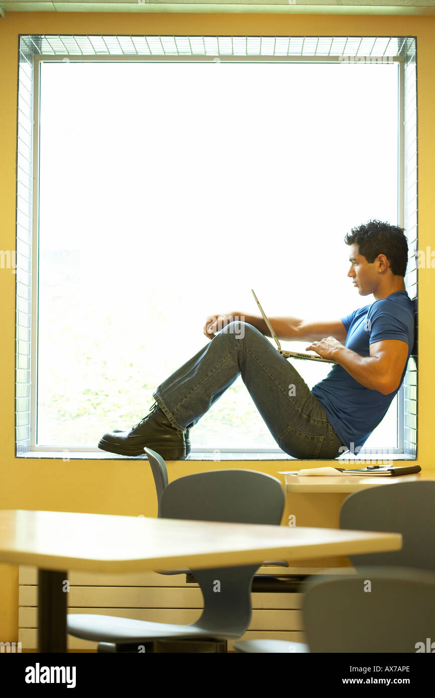 Side profile of a college student sitting on a window ledge and using a ...